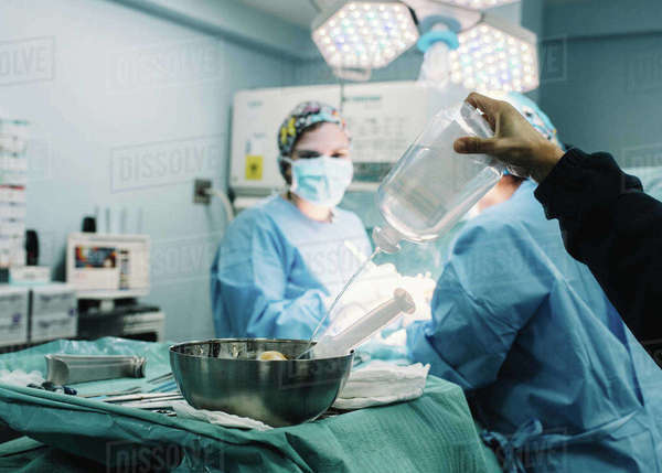 Crop hand pouring saline solution into bowl with syringe while doctors ...