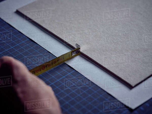 Hand of craftsman using steel ruler to measure paper border for folding ...