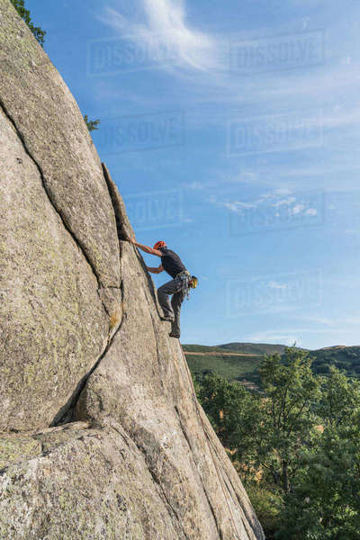 From below man climbing a rock in nature with climbing equipment ...