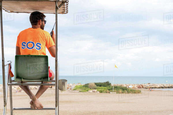 Back view of unrecognizable male employee on lifeguard tower speaking ...