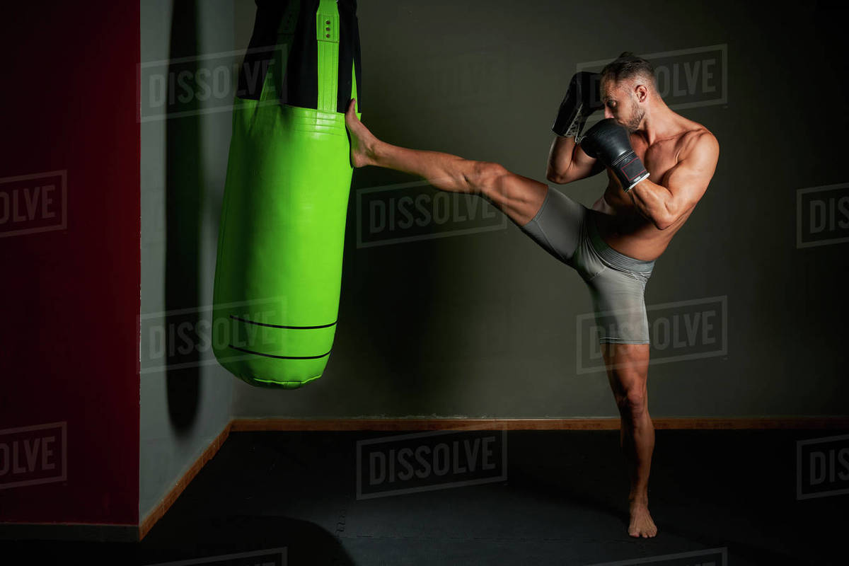 Full length of enduring shirtless male kickboxer in boxing gloves ...