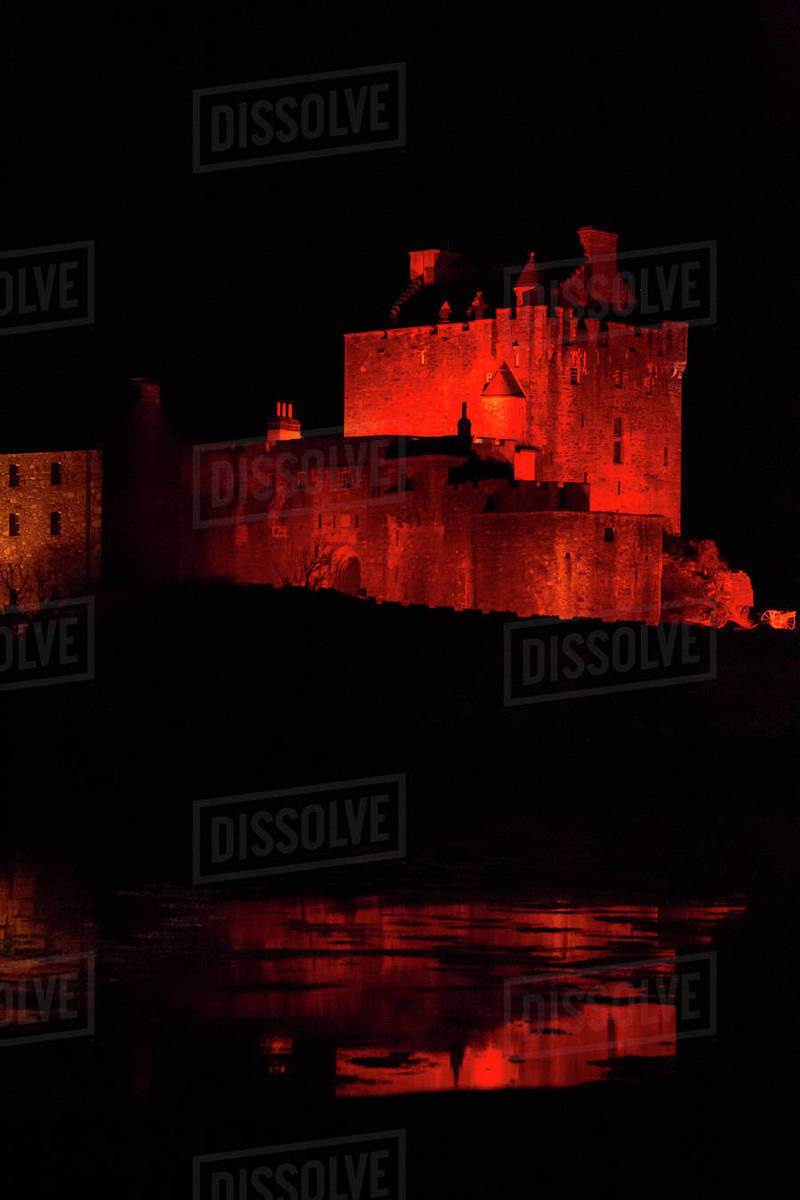 Night landscape of old majestic castle on river bank illuminated by red ...