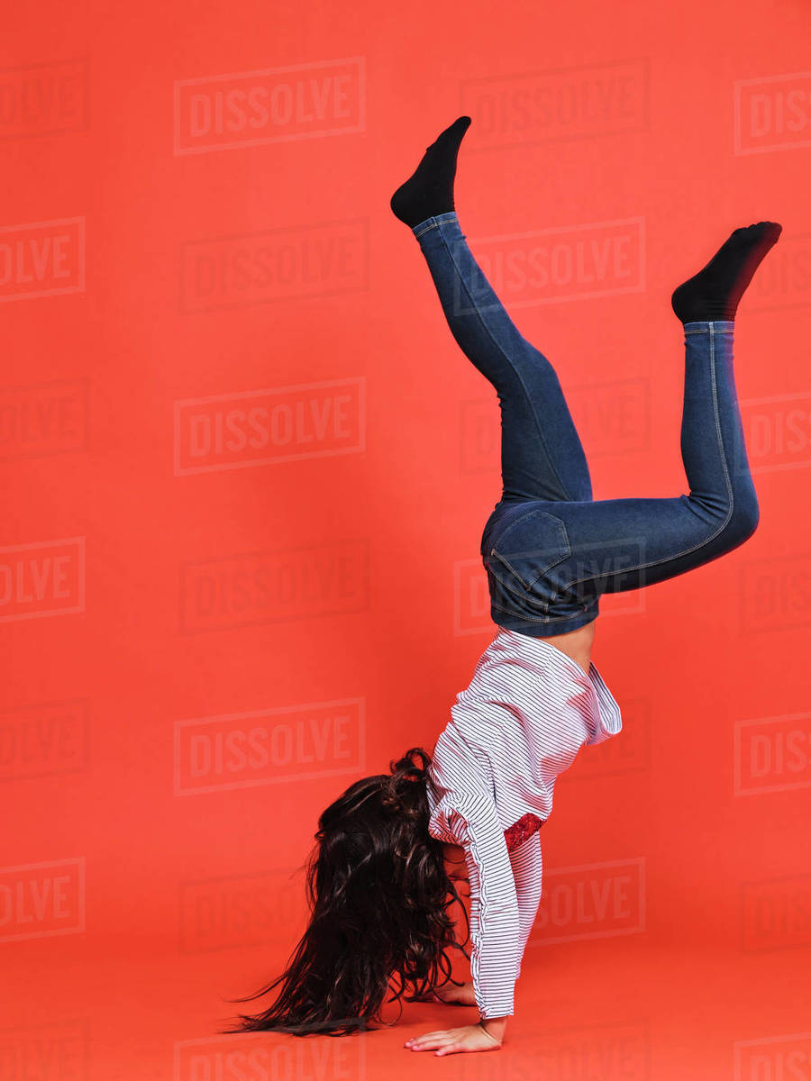 Side view of teen girl in jeans and blouse performing handstand against ...