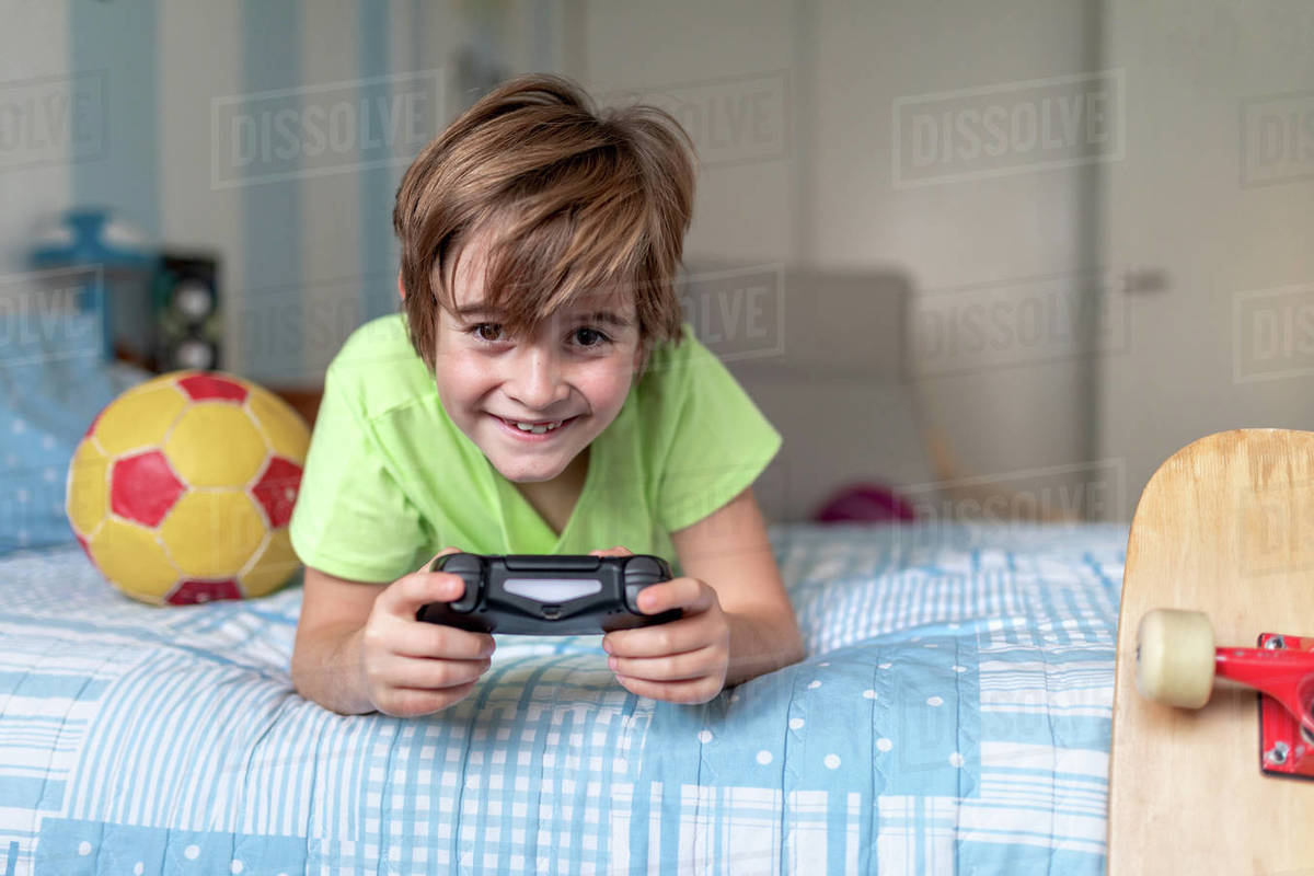Cheerful little boy spending time at home and playing video game while ...