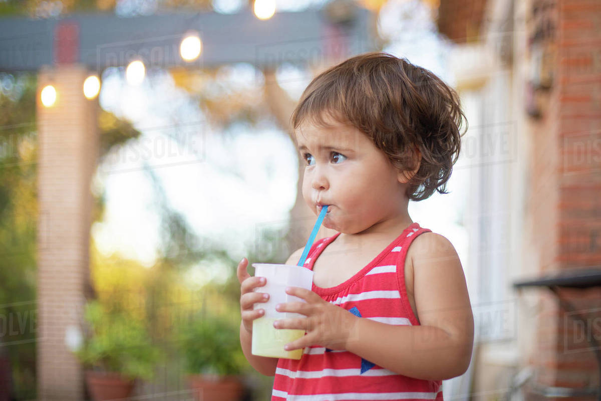 Cute little child sipping fresh beverage through straw and looking away ...