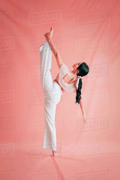 Back view of slim female in white outfit doing splits while dancing ...