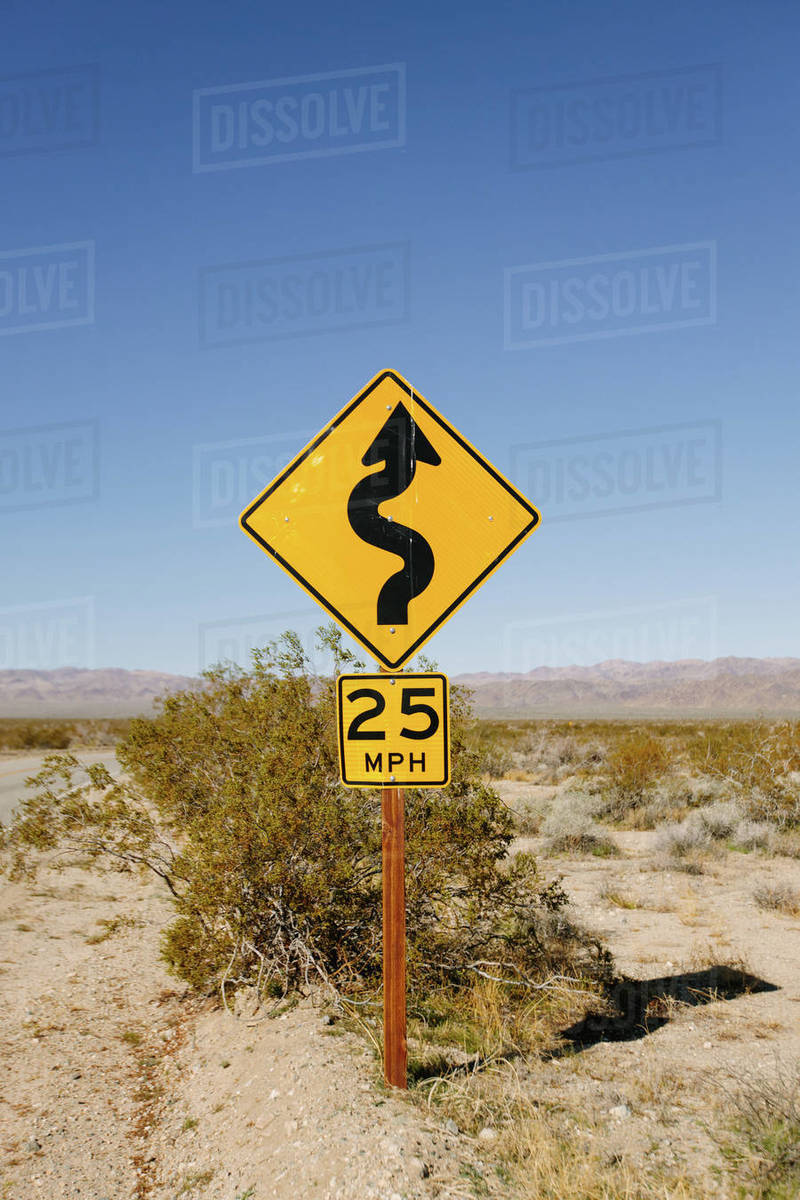 Yellow speed limit road sign locating in sandy area surrounded by dry ...
