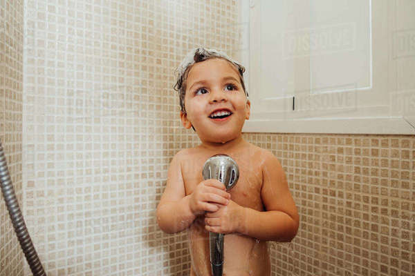 Smiling little child with foam on head standing in bathroom with shower ...