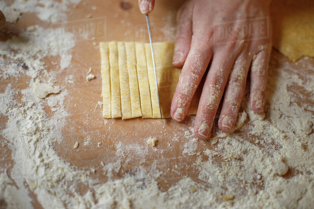 Faceless cook cutting dough into thin strips by knife on wooden table ...