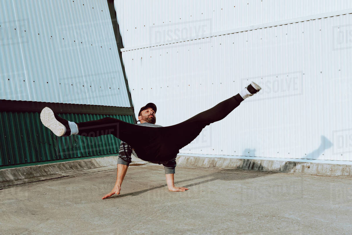 Side view of barefoot guy in stylish outfit performing flip near wall ...