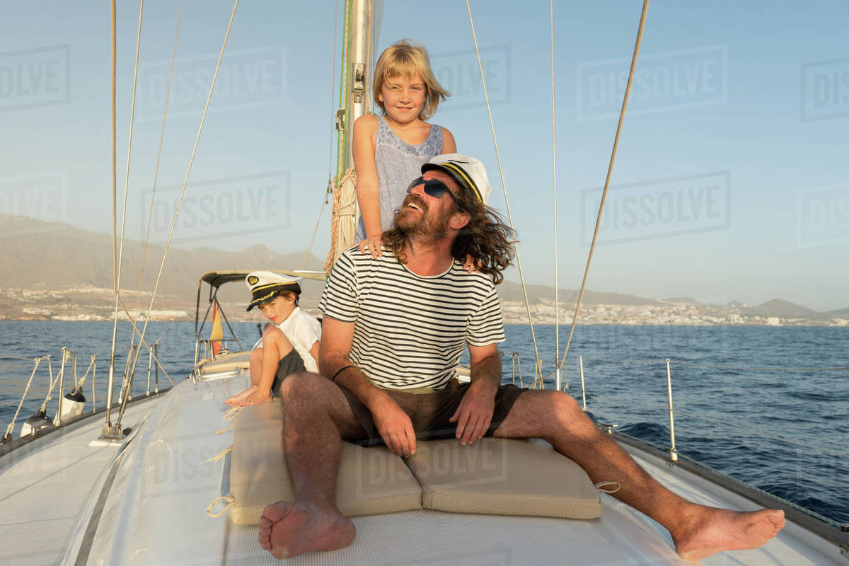 Positive father with happy kids in captain hats and sitting on deck of ...
