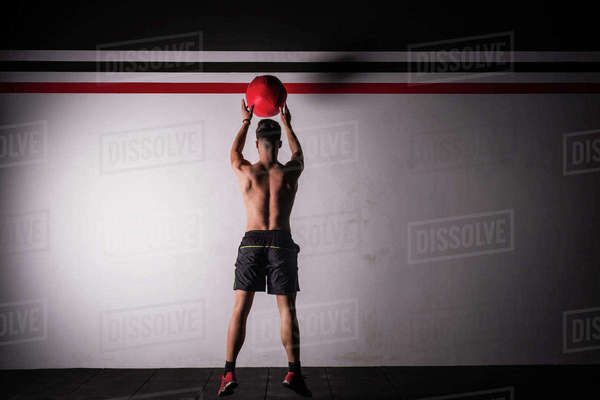 Back view of athletic young shirtless guy jumping and tossing big ball ...