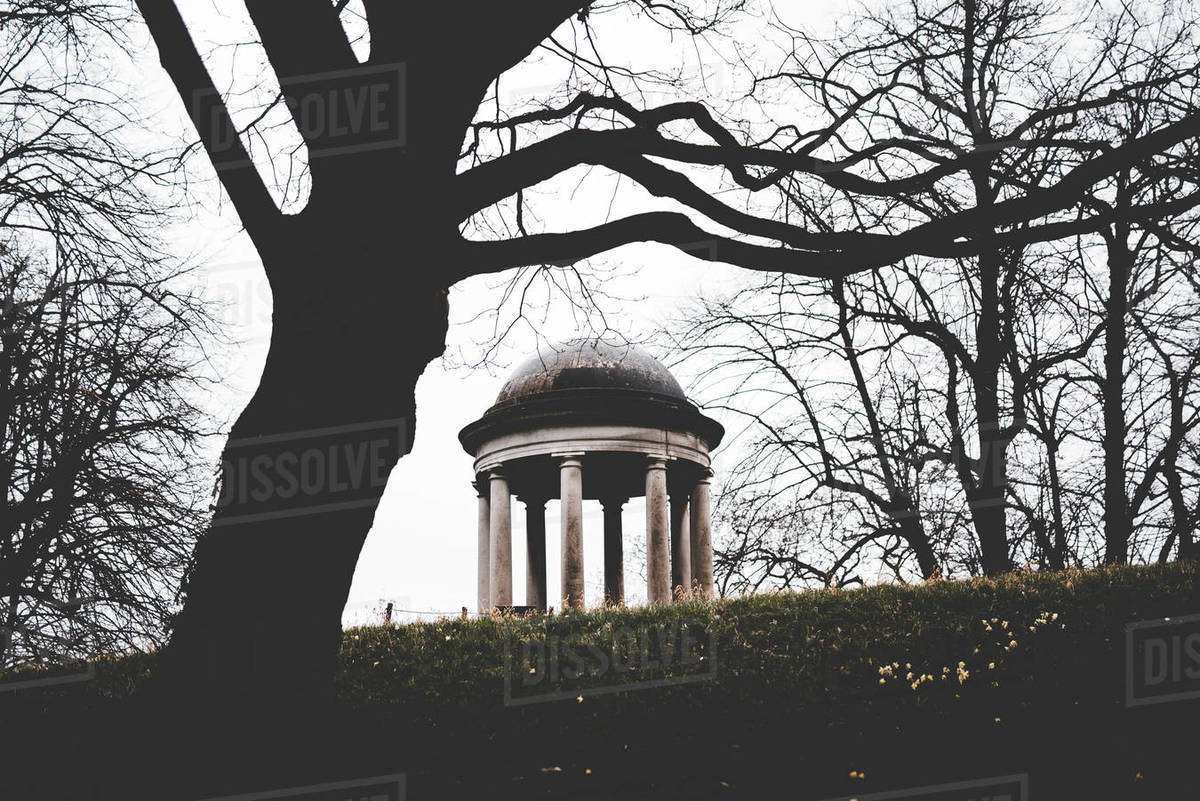 Aged round rotunda near dry trees in murk city garden in London ...