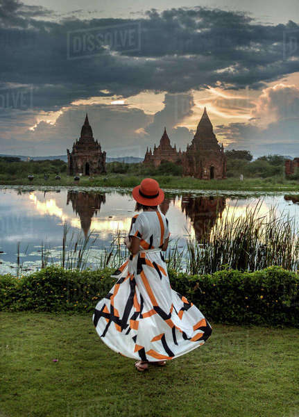 Back view of woman traveler in hat and dress standing on wooden deck at ...