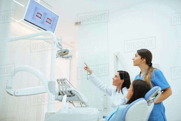 Side view of patient in chair and dentist with assistant in uniform ...