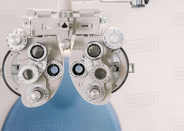 Modern vision test equipment and chair against white wall in optician ...