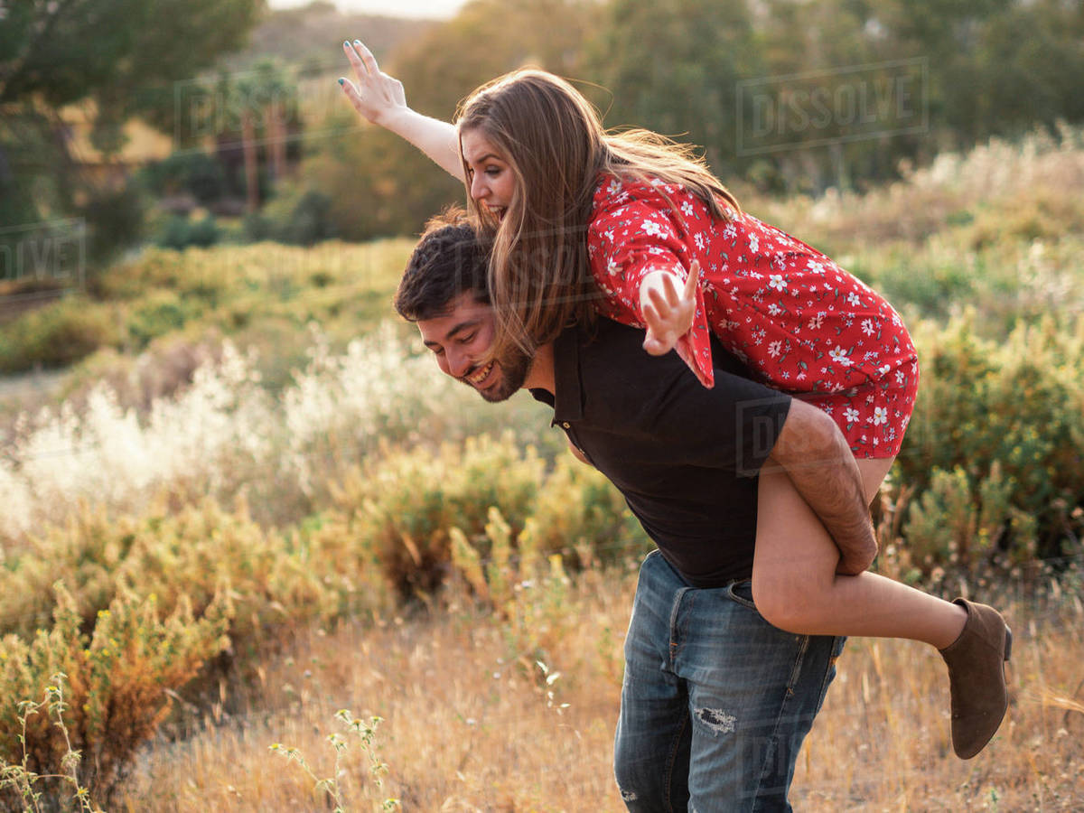Side view of cheerful couple playing piggyback while standing among ...