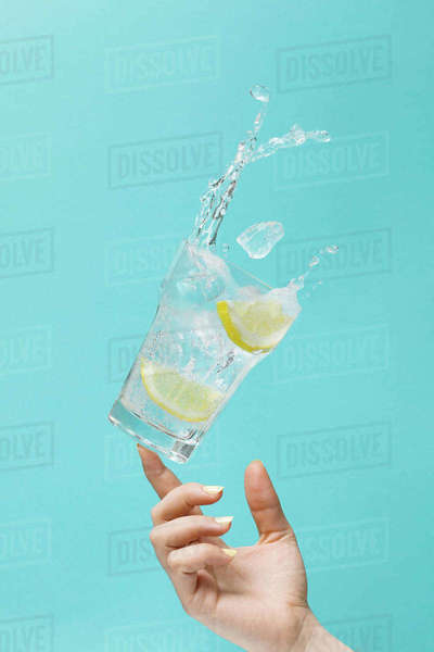Unrecognizable female tossing glass of fresh water with ice and lemon ...