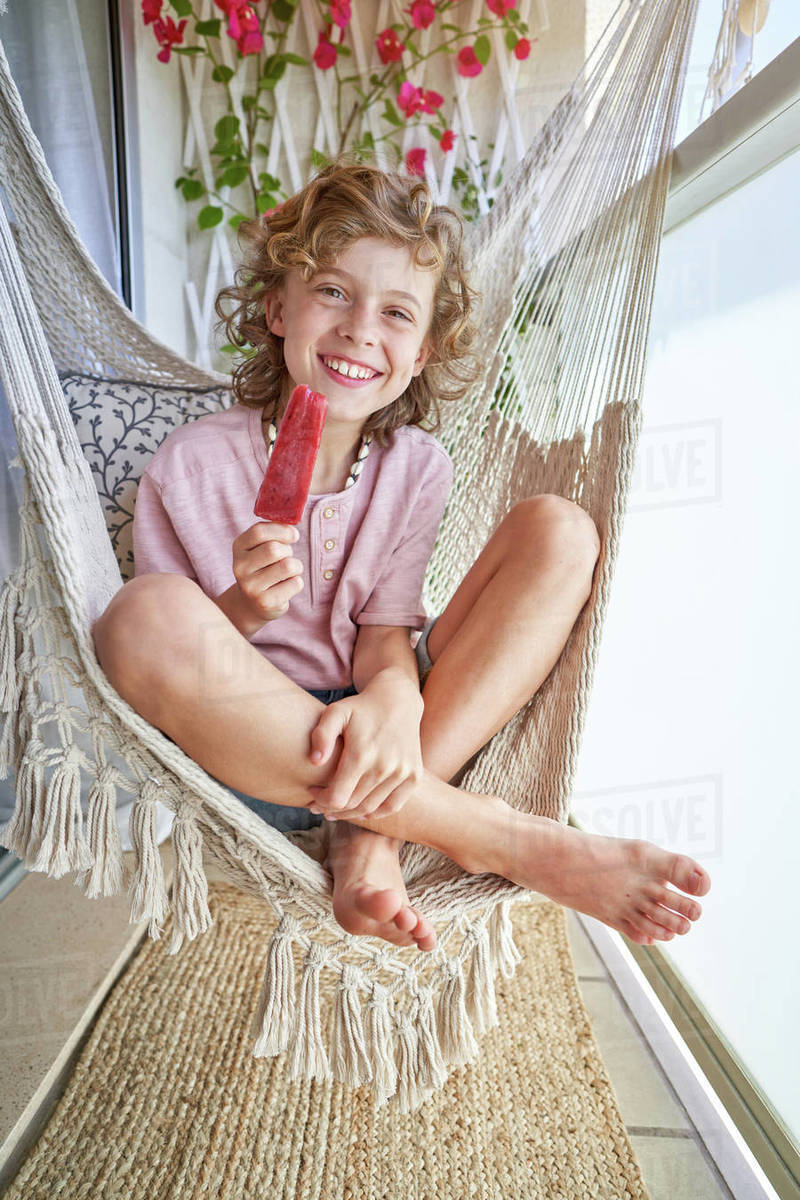 From above of barefoot blond boy resting in hammock with crossed legs ...