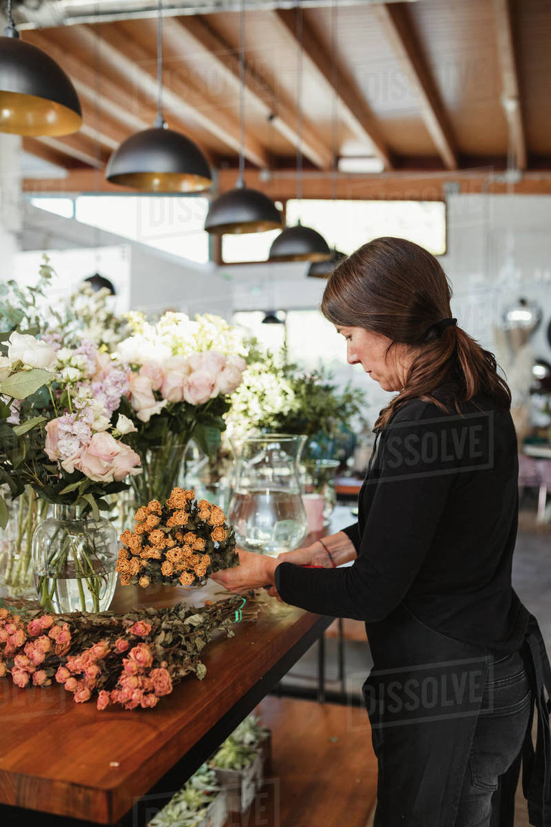 Side view of adult female floristry shop worker standing at wooden ...