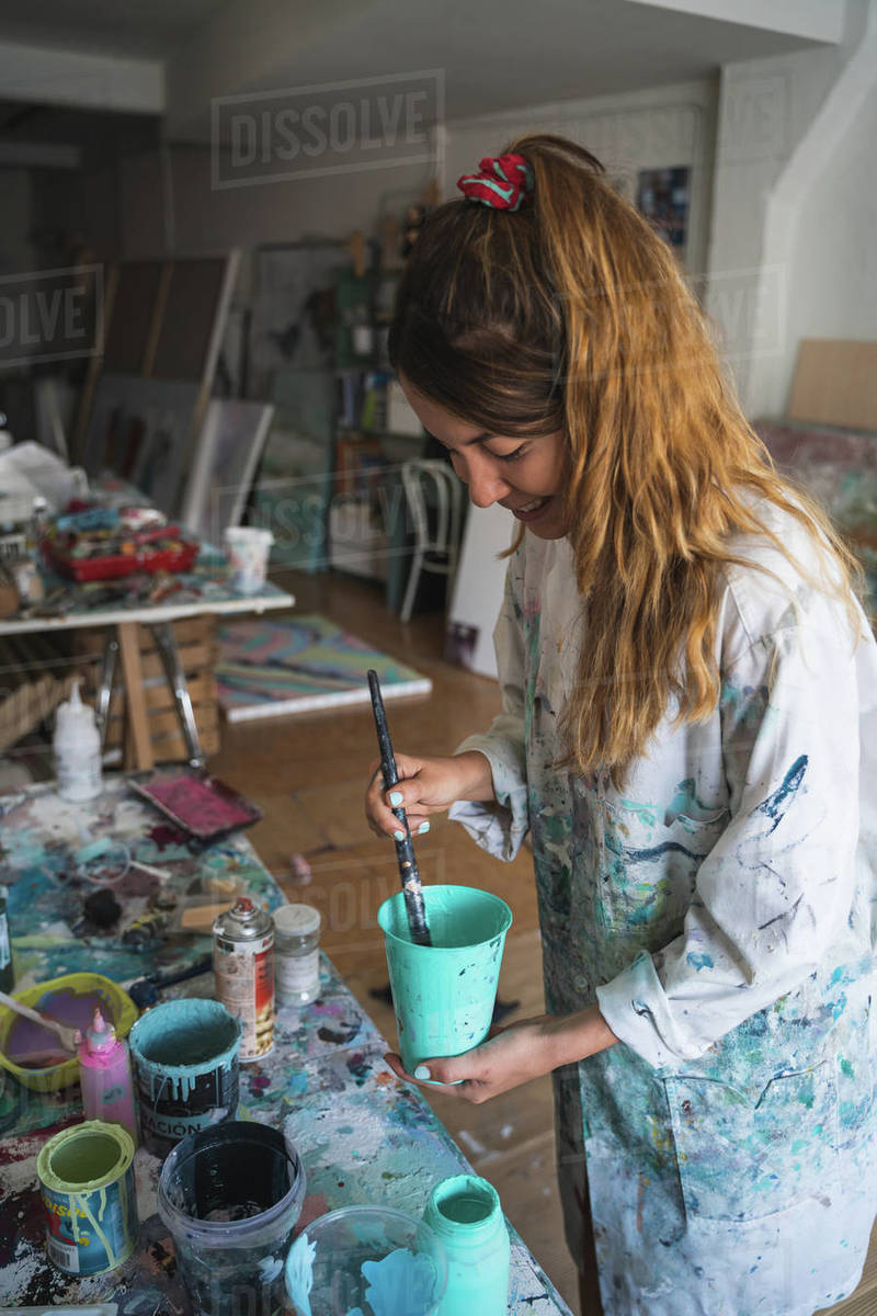 Side view young female artist standing at counter with various tools ...