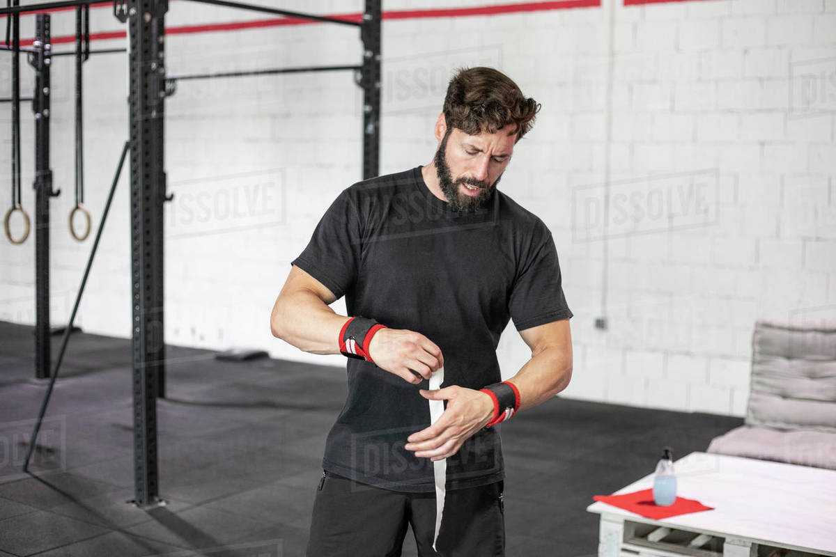 Professional male weightlifter standing in gym and taping fingers while ...