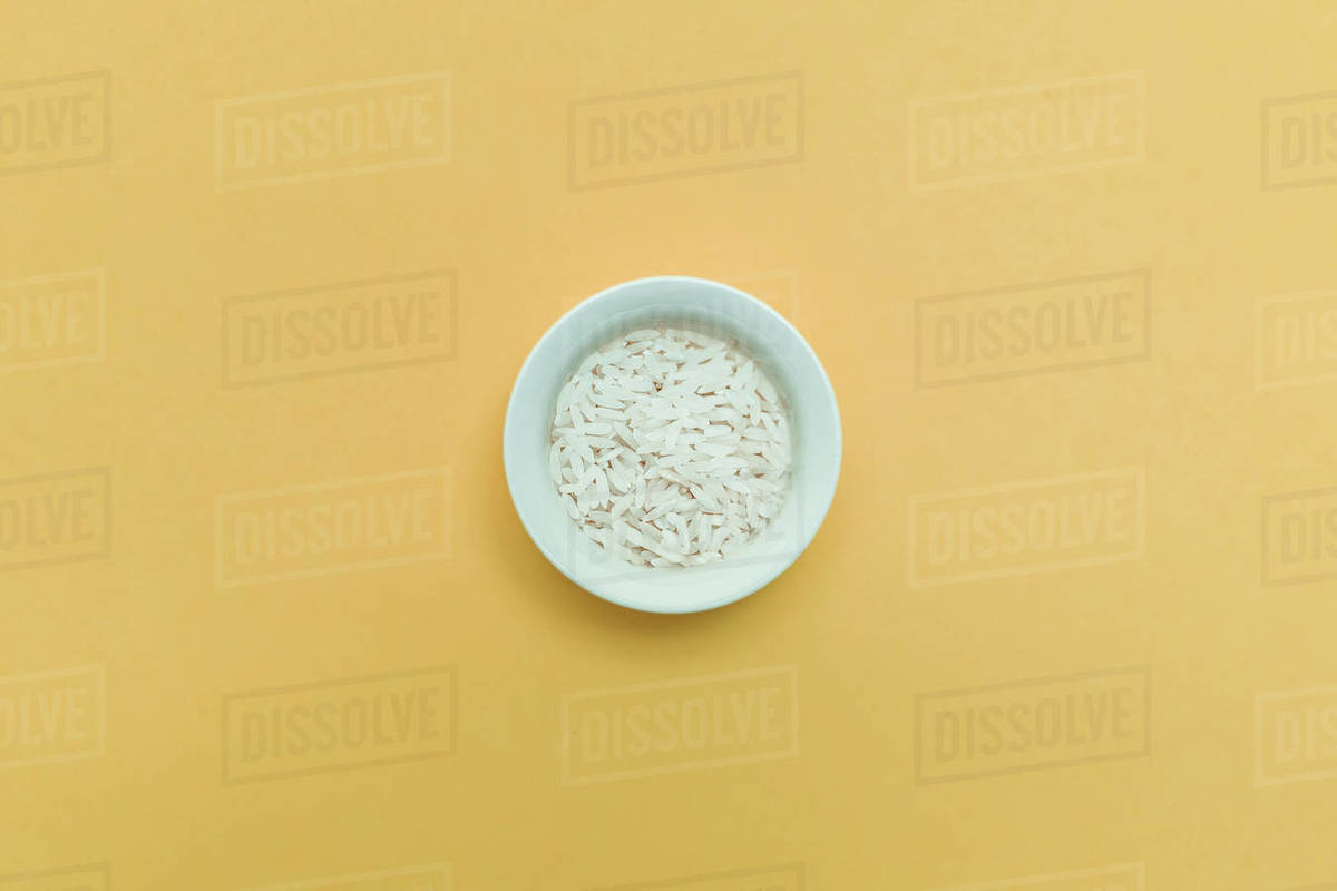 Top view of ceramic bowl of rice placed on yellow background in studio ...
