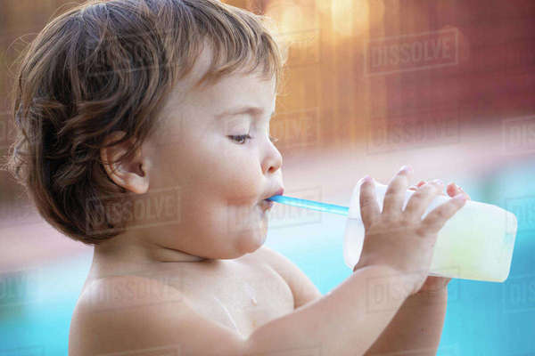 Side view of cute little child sipping fresh beverage through straw and ...