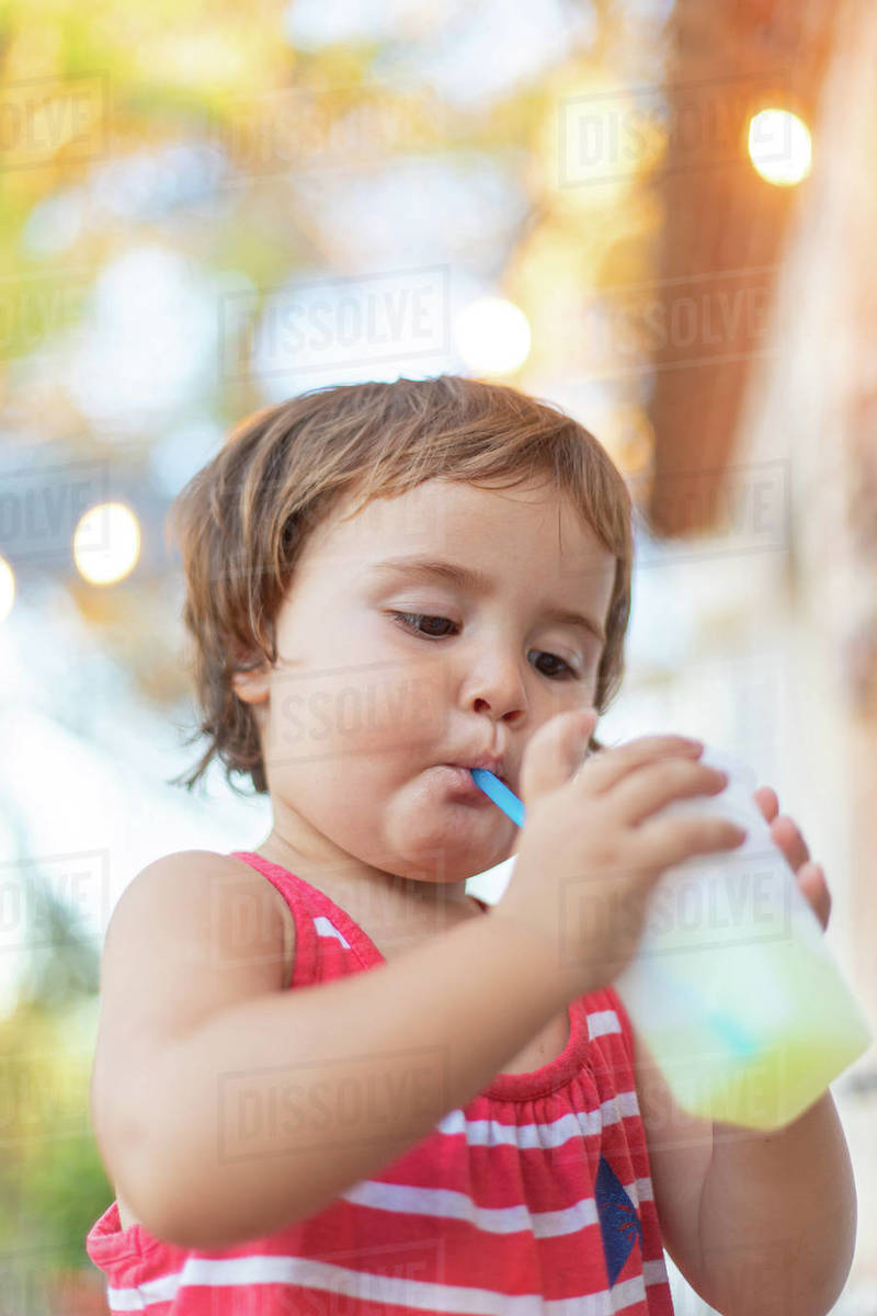 Cute little child sipping fresh beverage through straw and looking away ...
