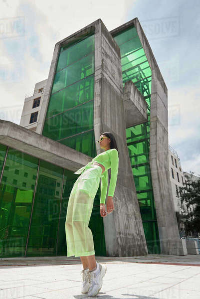 Low angle side view of female model in trendy wear standing on tiptoes ...