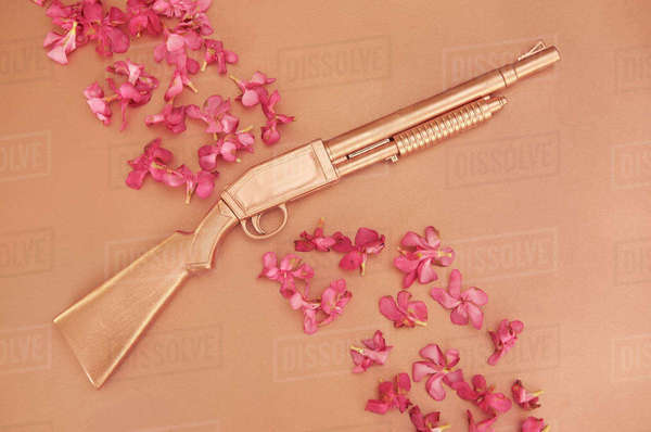 Top view of golden shotgun placed with flower petals on pink background ...