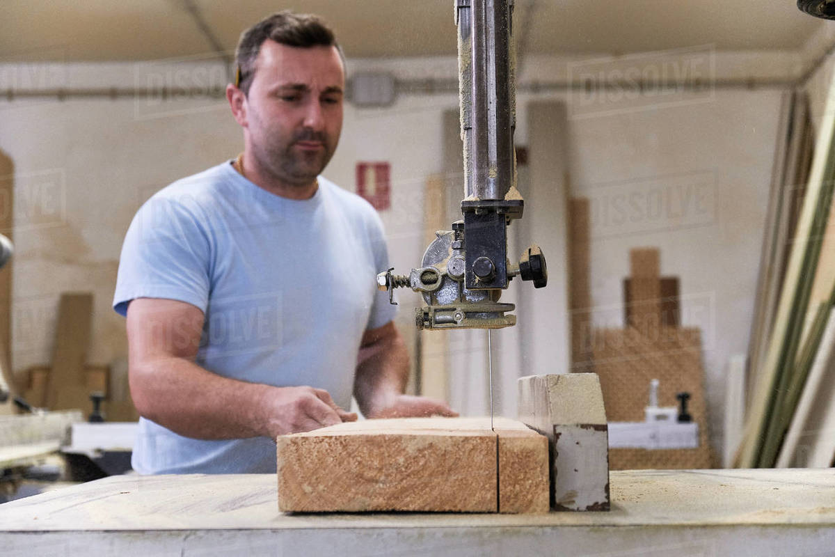 Low angle of male woodworker in casual clothes focusing and cutting ...