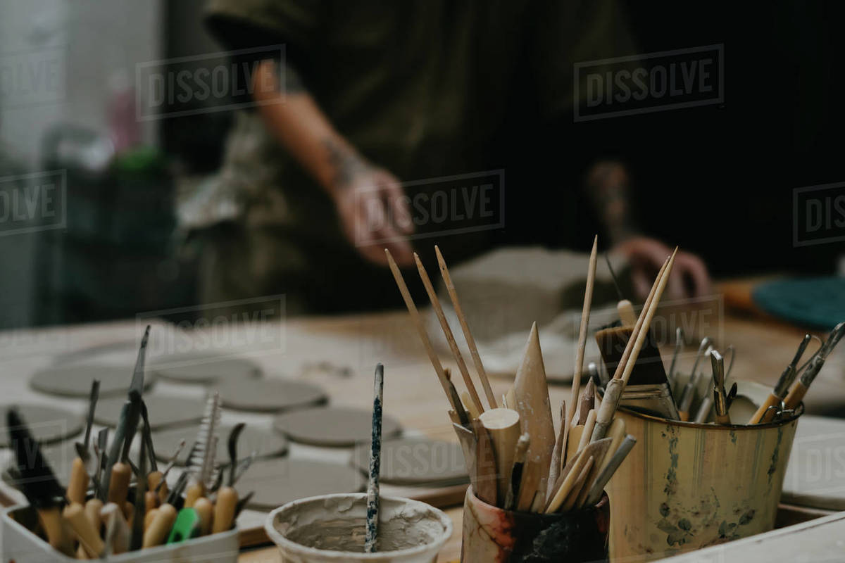 Various instruments for pottery placed on dirty workbench on blurred ...
