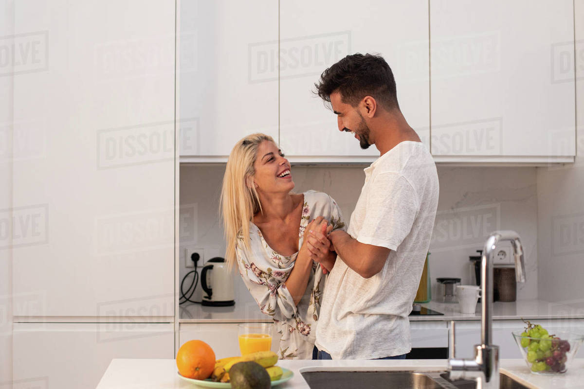 Side view of smiling couple cuddling in modern kitchen during breakfast ...