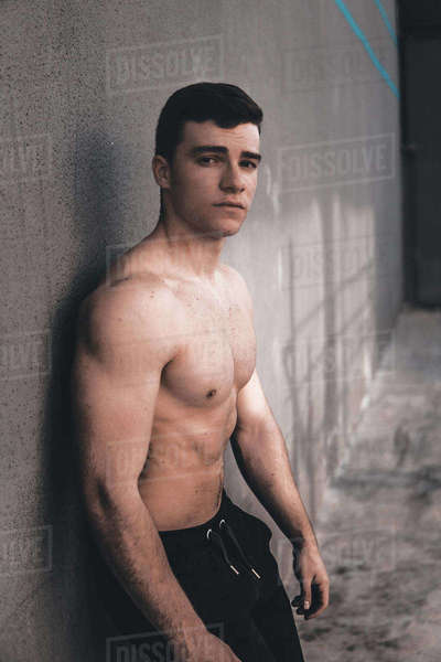 Side view of muscular shirtless guy looking at camera while leaning on ...