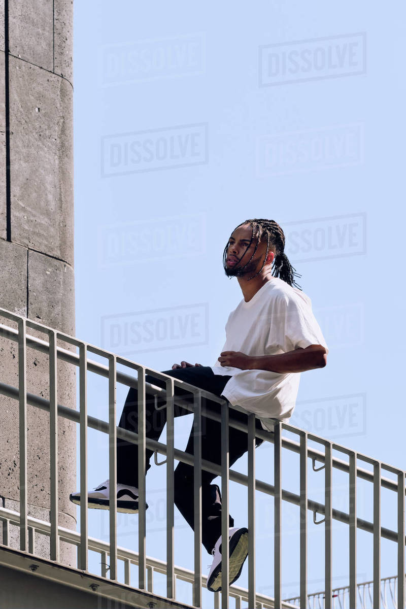 Young African American man sitting on railing of bridge while spending ...