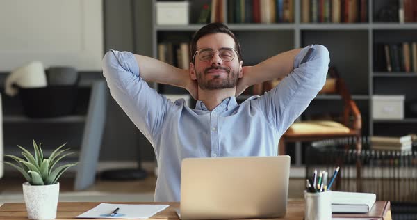 Satisfied employee relaxing at office desk holding hands behind head ...