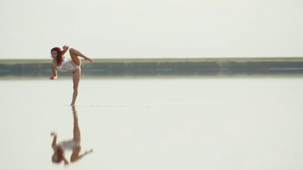 Flexible woman in white bathing suit is doing gymnastics in the water ...