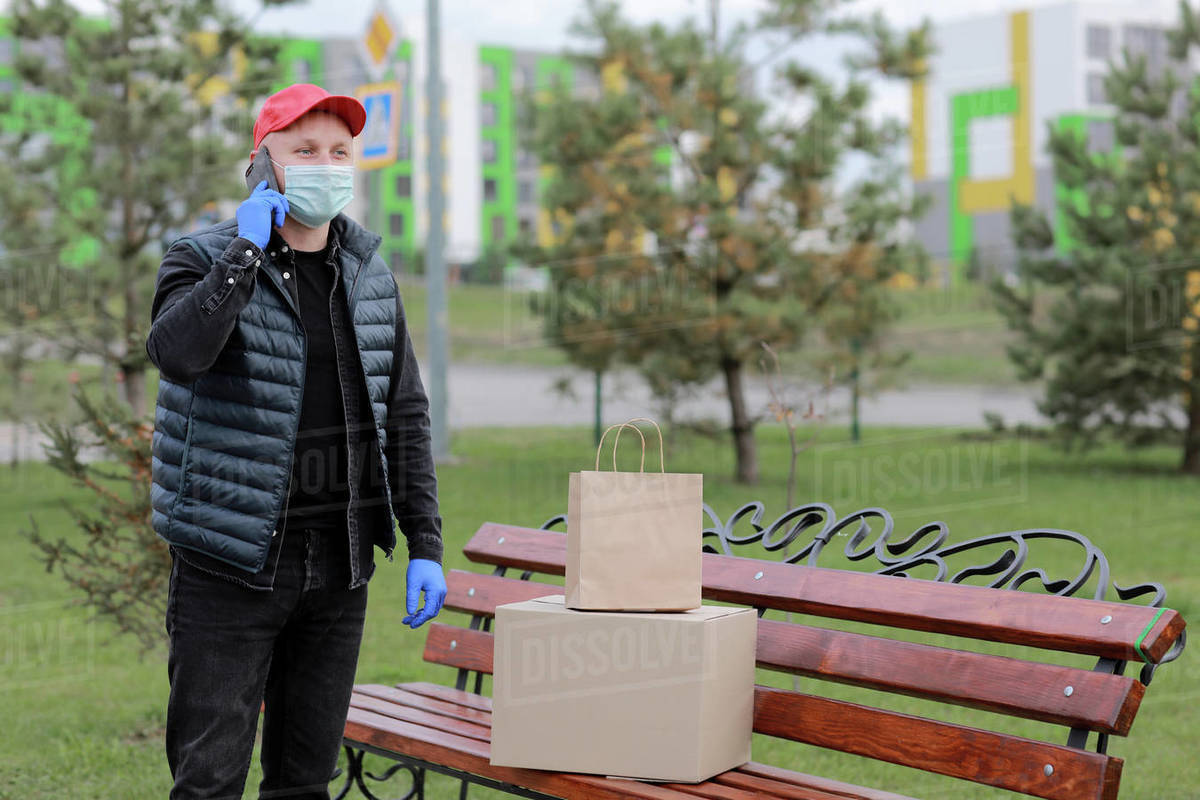 Delivery man in red hat, protection mask and medical rubber gloves with ...