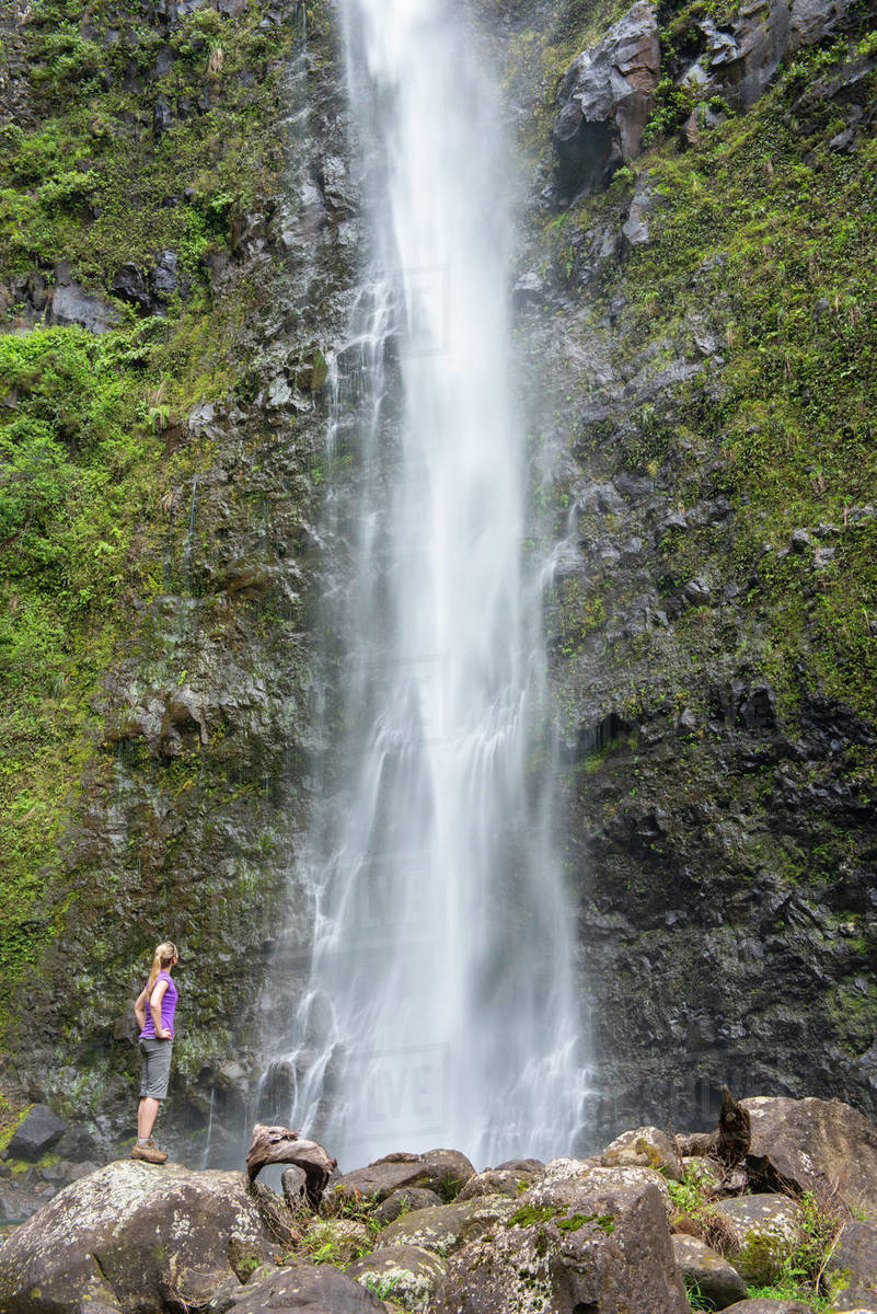 Hiker admiring a waterfall along the famous Kalalau Trail, along Kauai ...