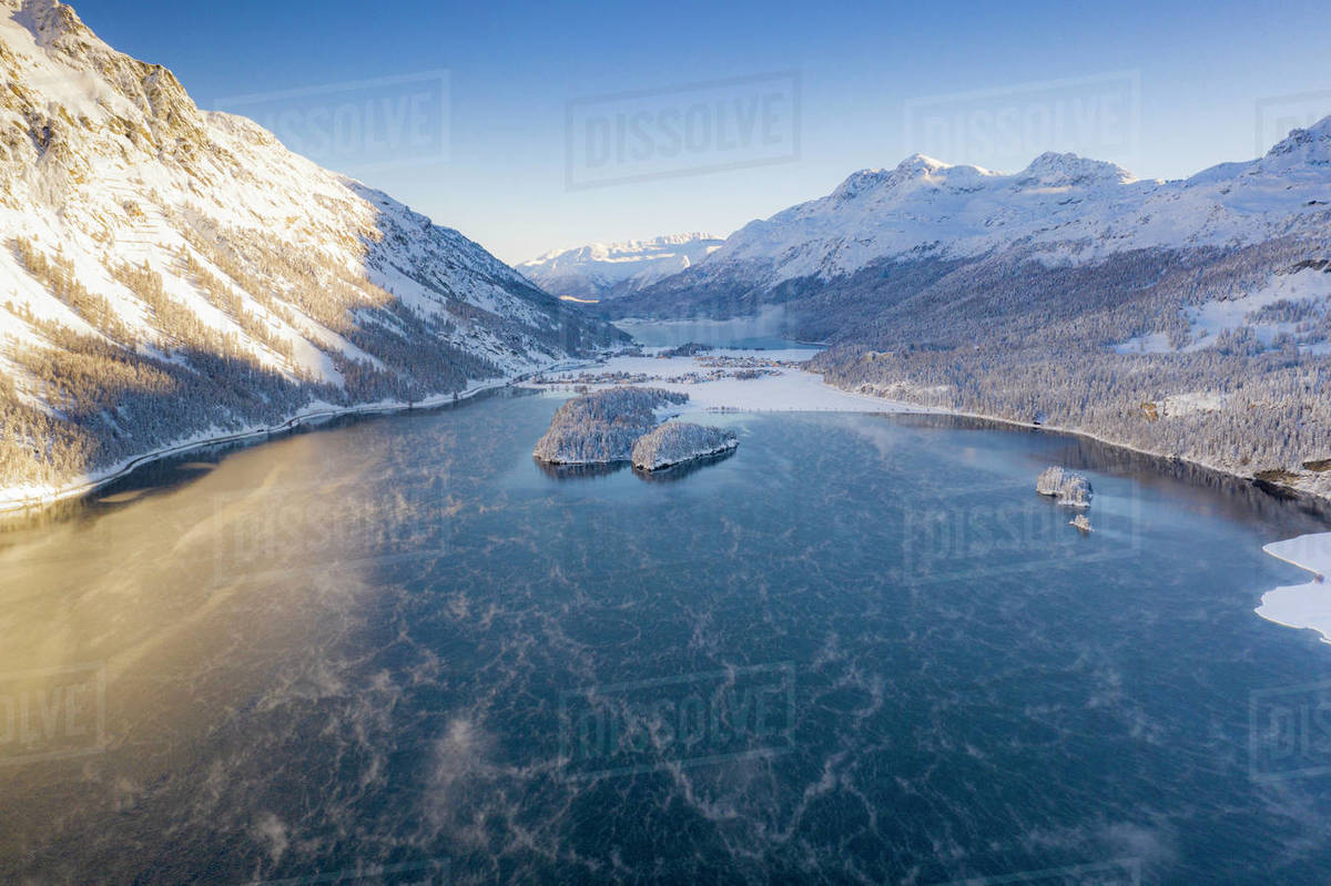 Snowcapped mountains frame the village of Sils Maria and frozen Lake ...