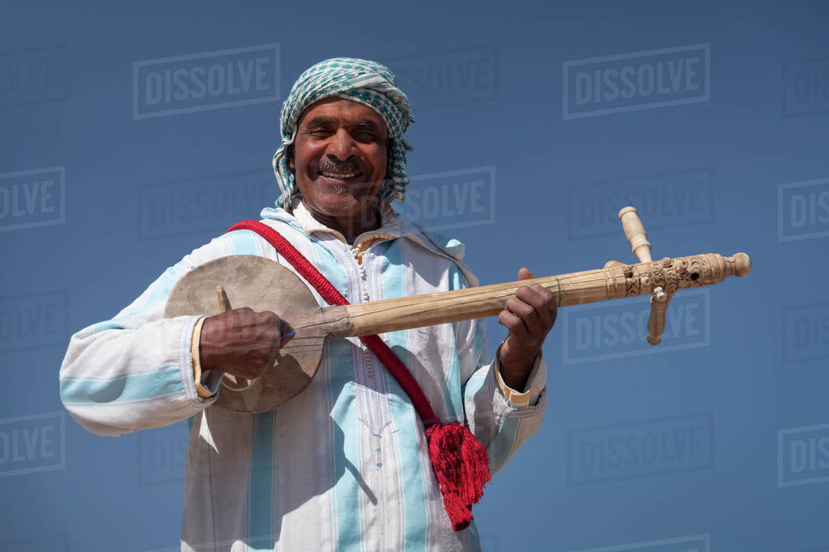 Moroccan man in traditional dress playing a traditional Gimbri ...