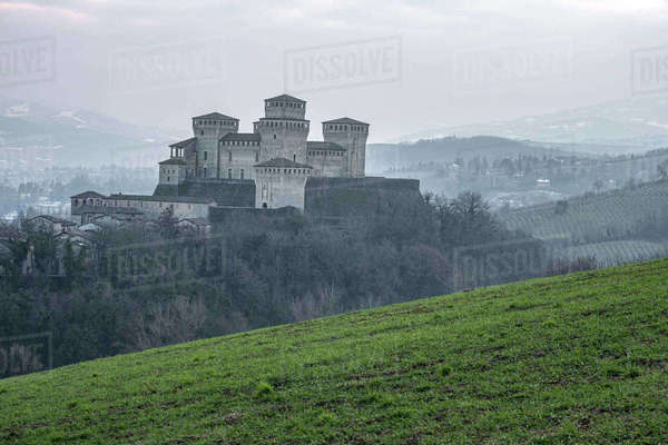 Medieval castle of Torrechiara with square towers on a hill on a foggy ...