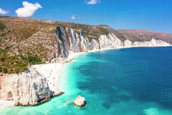 Tourists sunbathing at idyllic Fteri Beach set among cliffs and blue ...