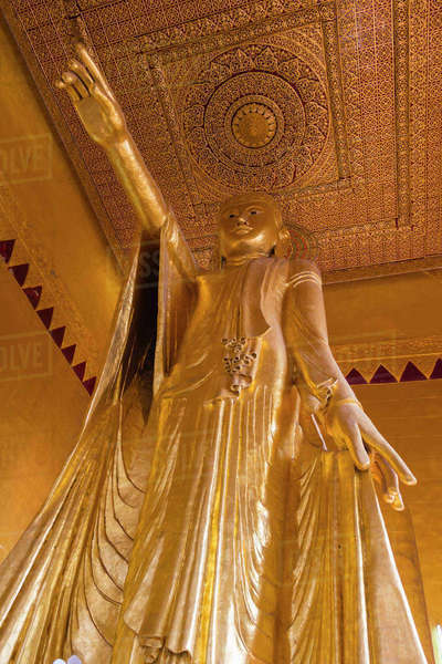 Standing gilded statue of Buddha pointing with his hand inside temple ...