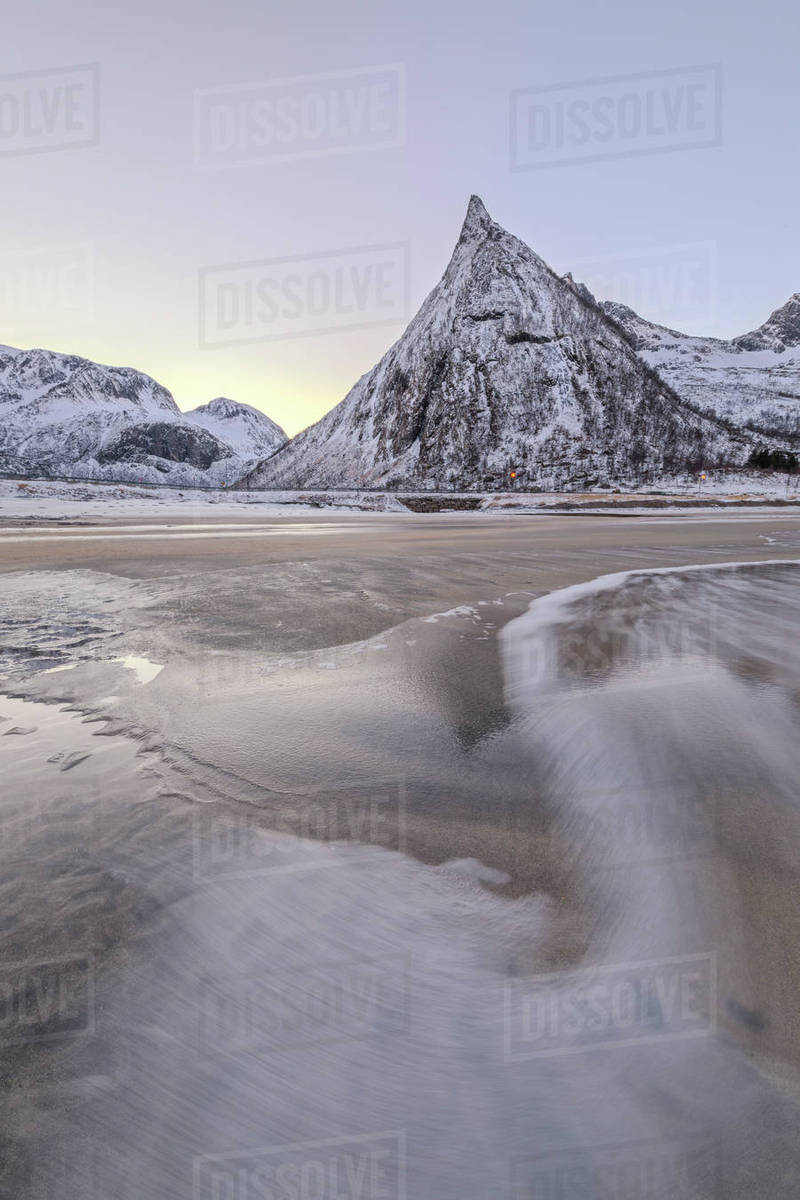 Snowy peaks and sandy beach framed by the icy waves of frozen sea at ...