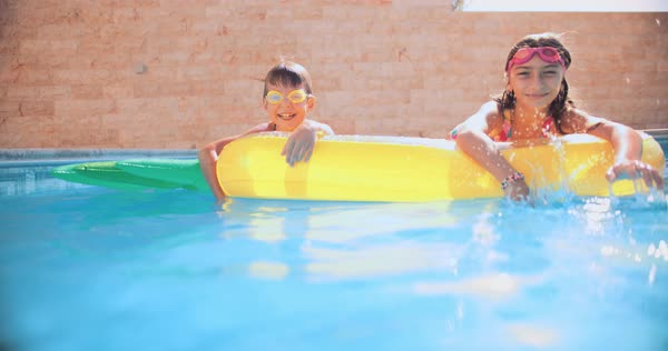 Young children splashing and floating on inflatable in swimming pool ...