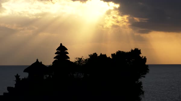 Sun rays above a silhouetted tanah lot temple on the island of bali ...