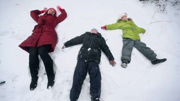 Mother with her kids boy and little girl lay on snow and move hands ...