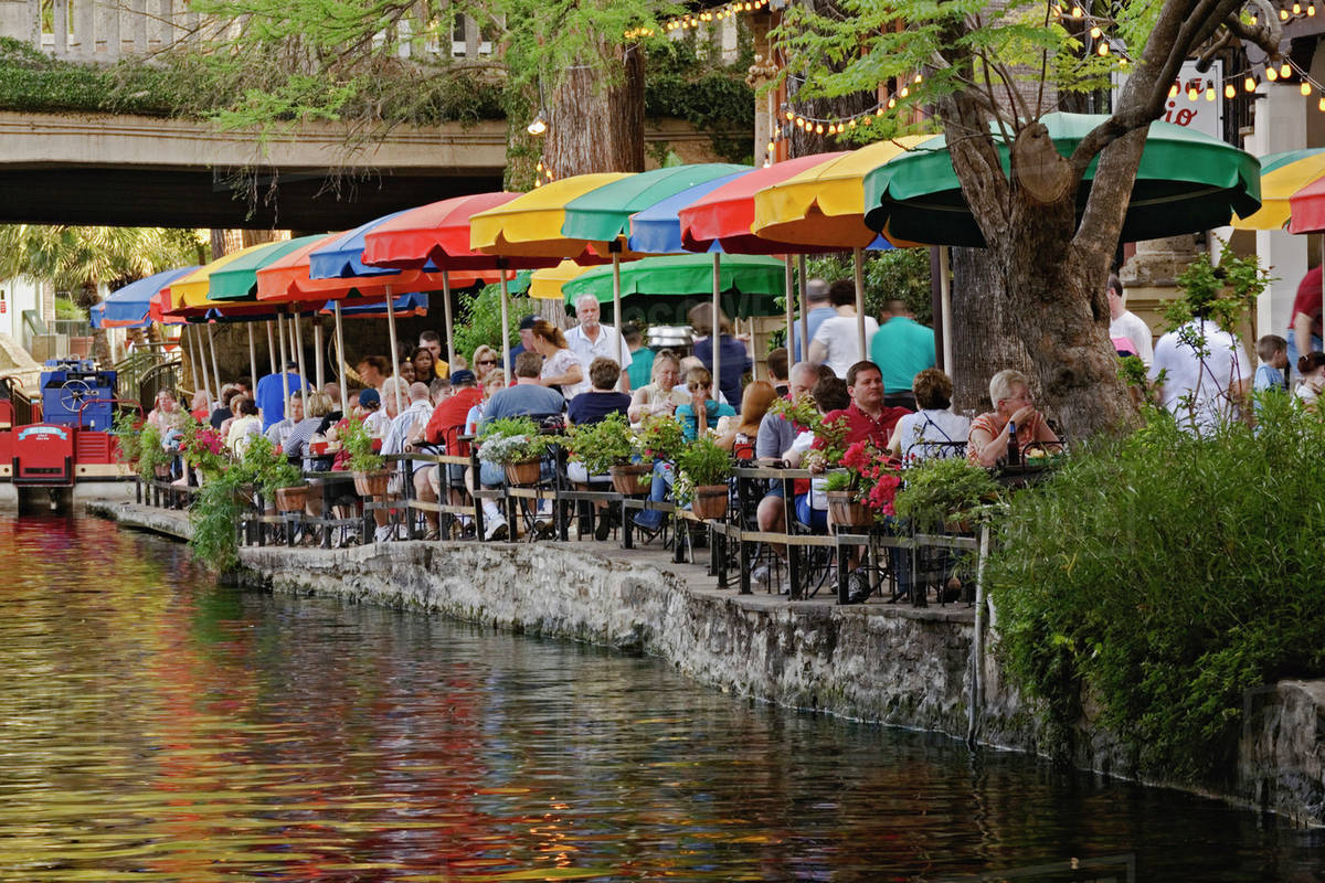 Colorful umbrellas and visitors dining in outdoor cafe along River Walk ...